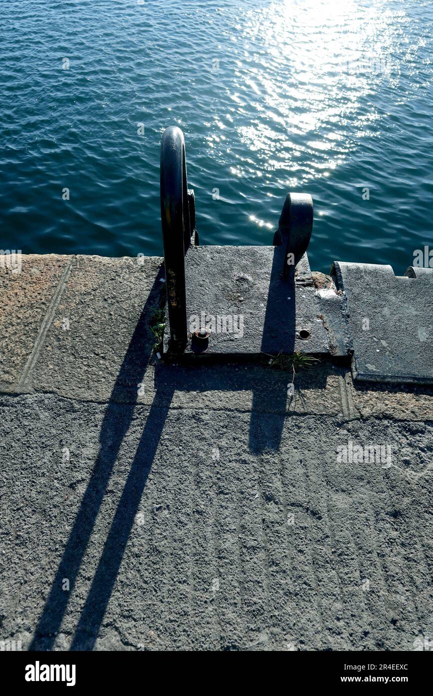 A person stands on the edge of a pier, looking out at the tranquil blue ...