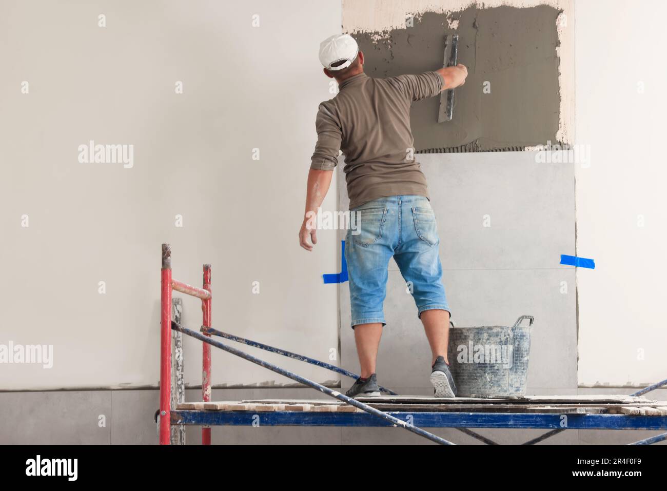 Worker spreading adhesive mix over wall for tile installation indoors ...
