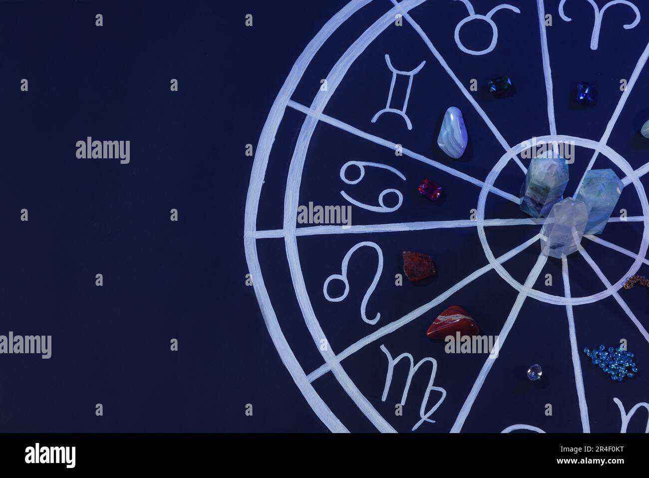 Natural stones for zodiac signs and drawn astrology chart on dark blue ...