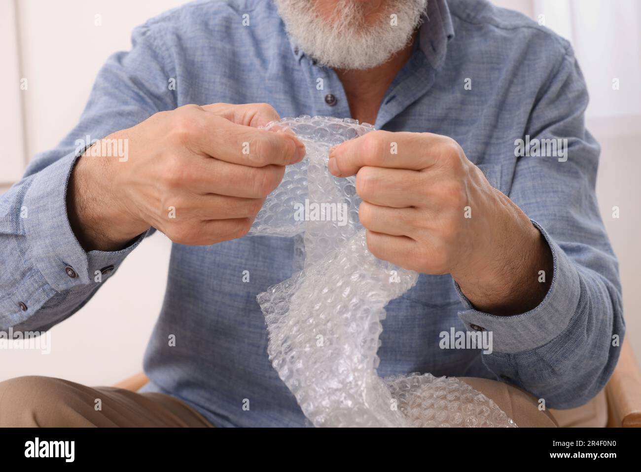 Senior man popping bubble wrap at home, closeup. Stress relief Stock ...