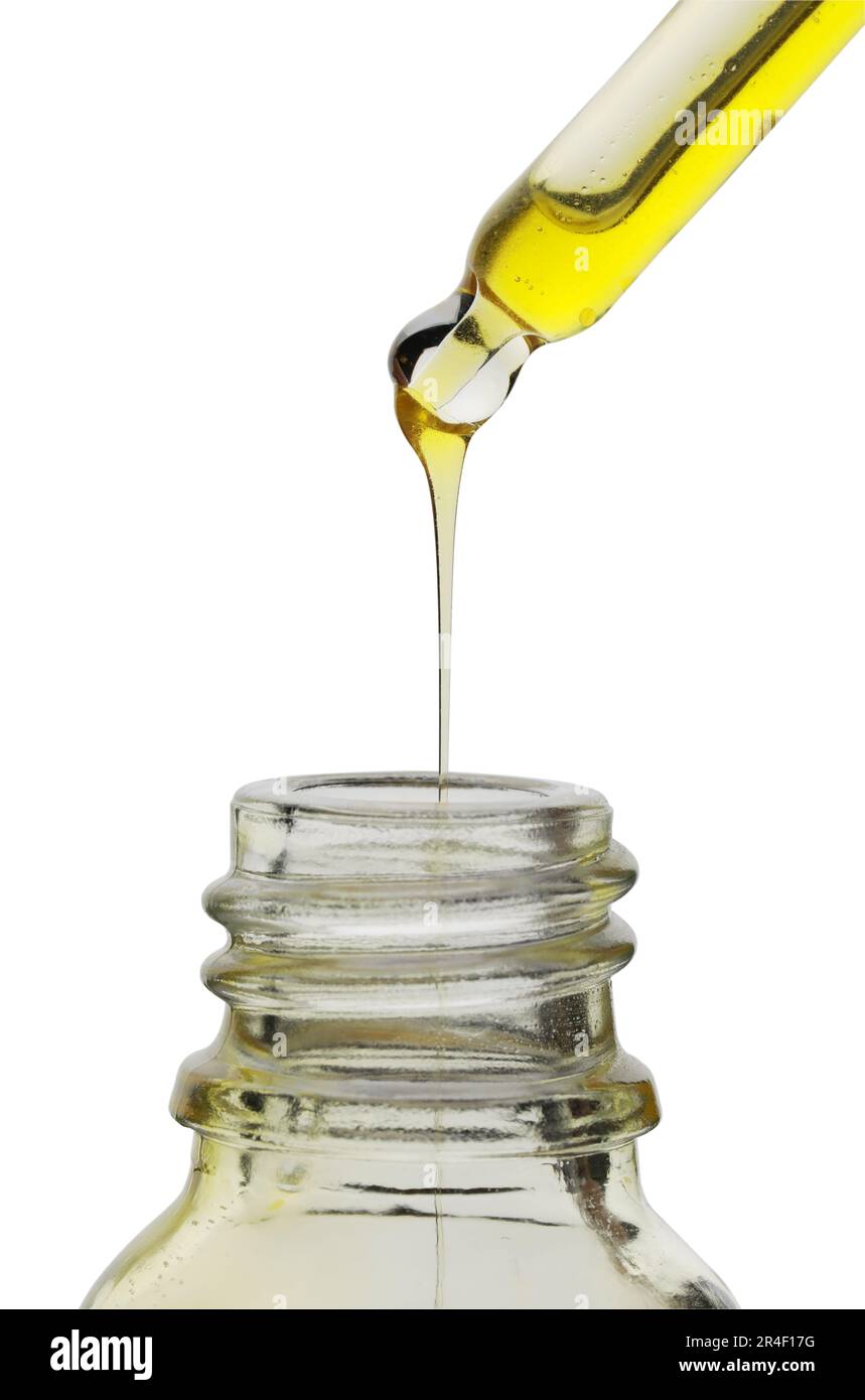 Dripping yellow facial serum from pipette into glass bottle on white ...