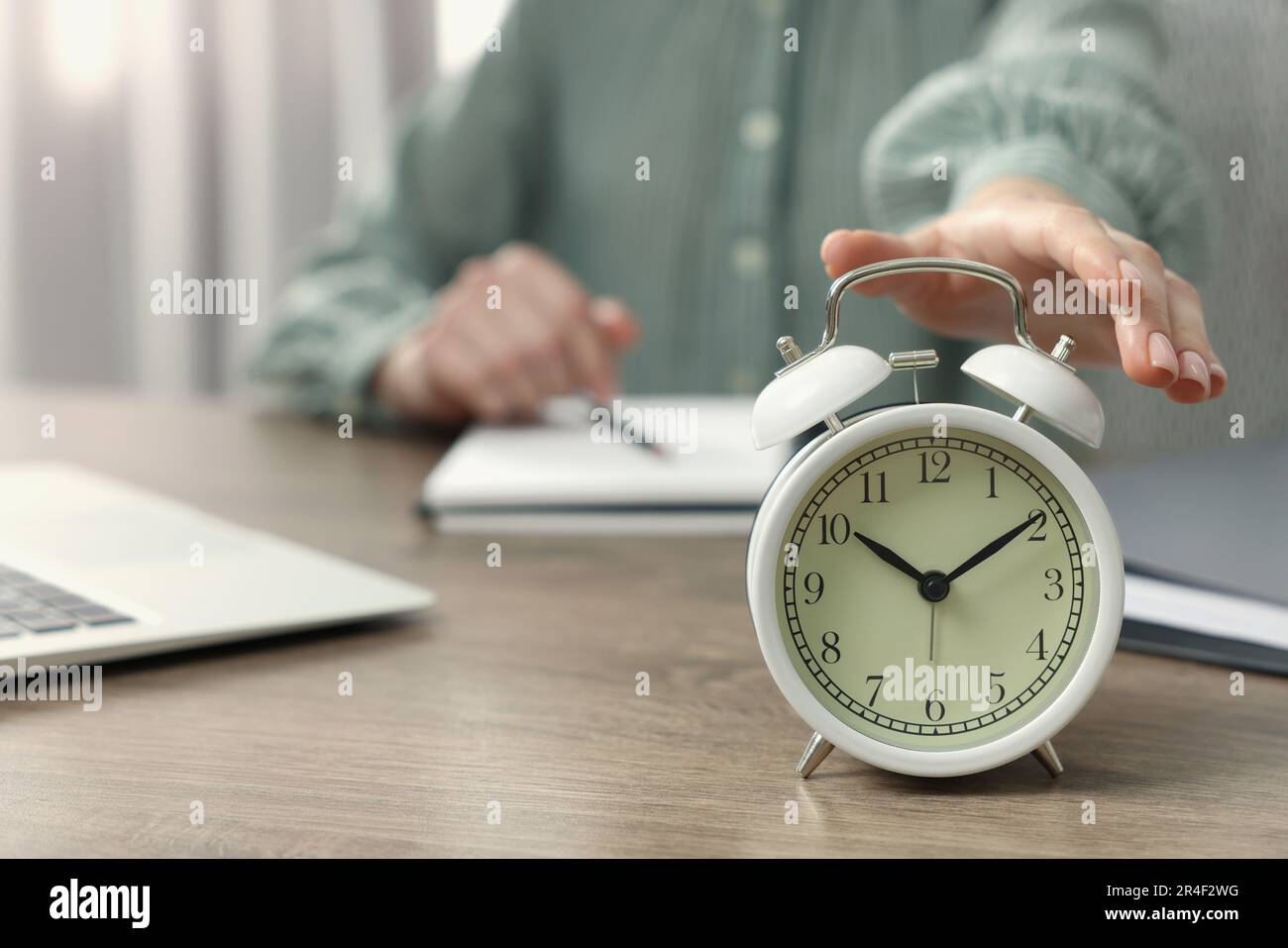 Woman turning off alarm clock at table, closeup. Space for text Stock ...