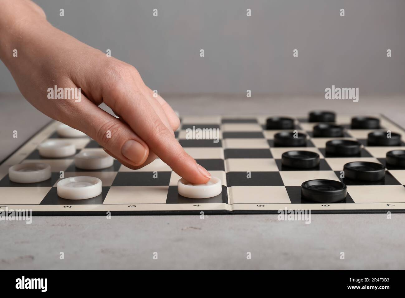 Woman moving checker on board at light grey table, closeup Stock Photo ...