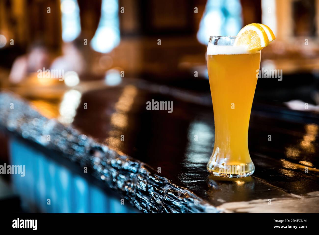 A glass of cold, orange-flavored beer is placed on the bar counter ...
