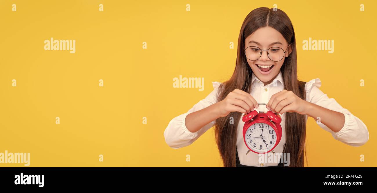 amazed child in school uniform and glasses with alarm clock showing ...