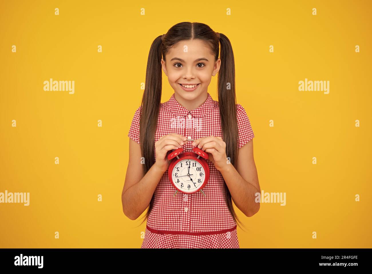 Teenager child hold clock isolated on yellow studio background ...