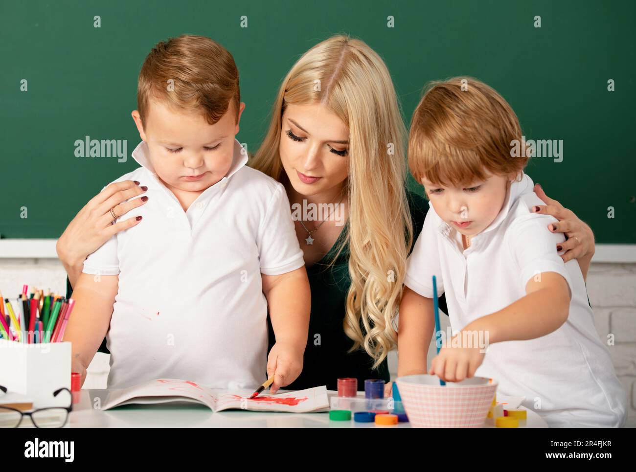 Children drawing in kindergarten. Teacher explains lesson to school ...