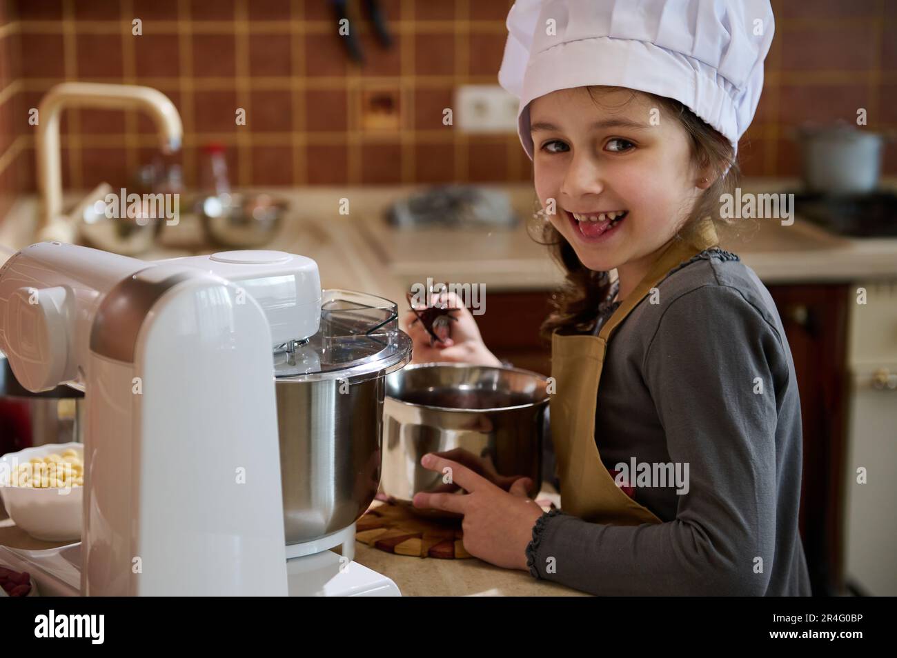 Adorale mischievous little child girl tasting melted belgian chocolate ...