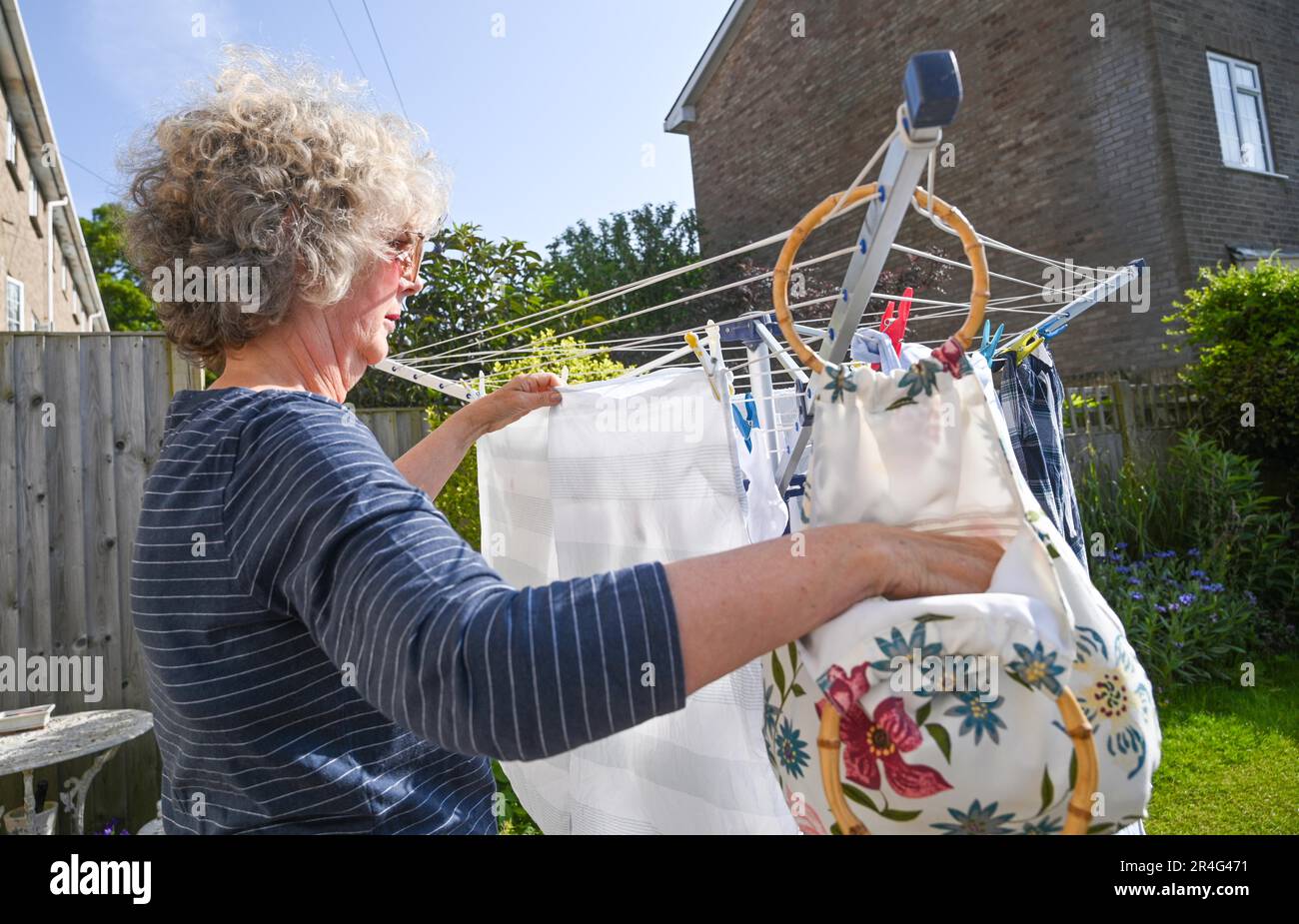 A woman pegs out her washing on a rotary washing line in a small urban ...