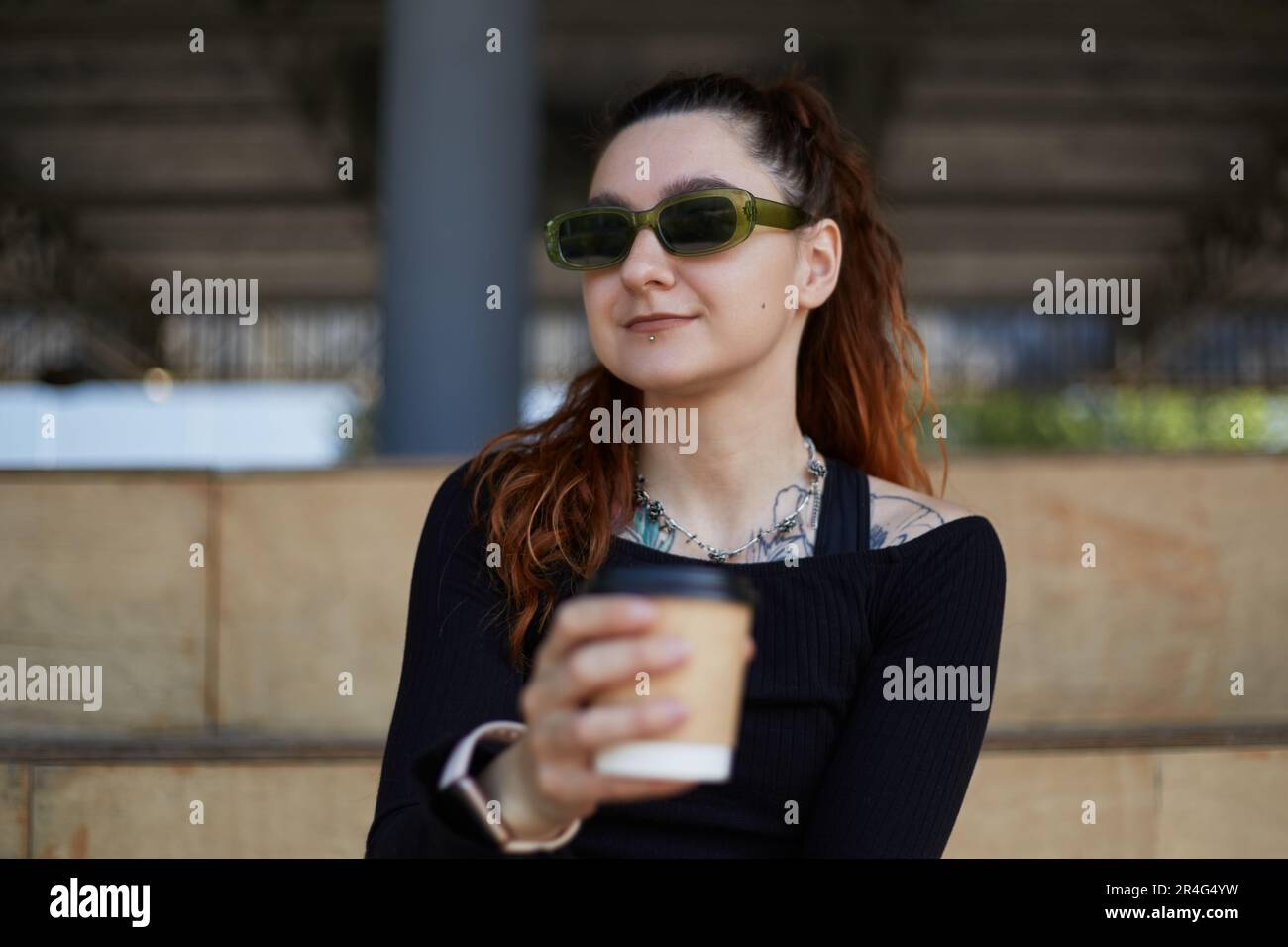 Cool young diverse female with tattooed chest posing with a cup of ...