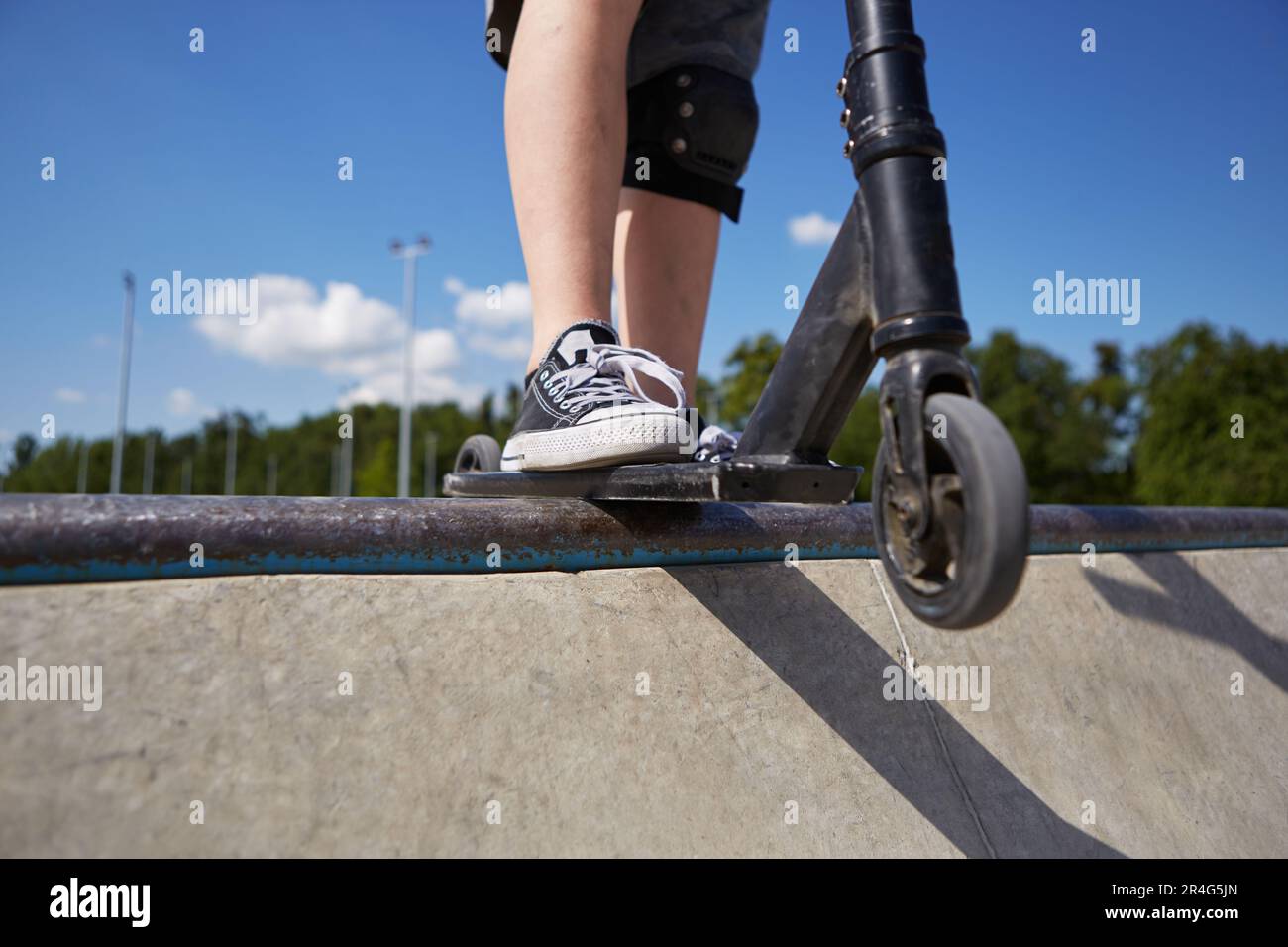 Young boy riding on a kick scooter in a concrete skatepark ...