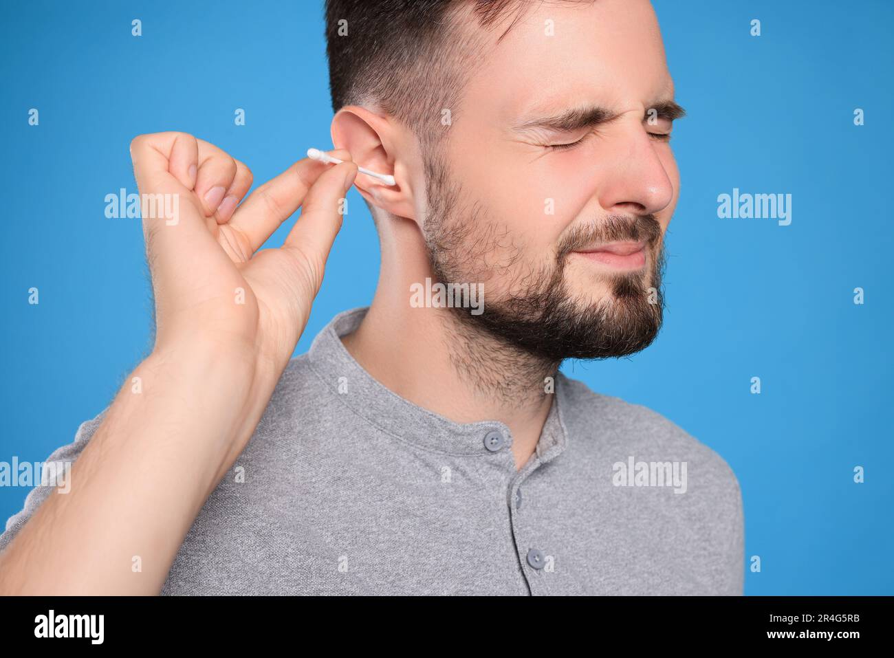 Young man cleaning ear with cotton swab on light blue background Stock ...