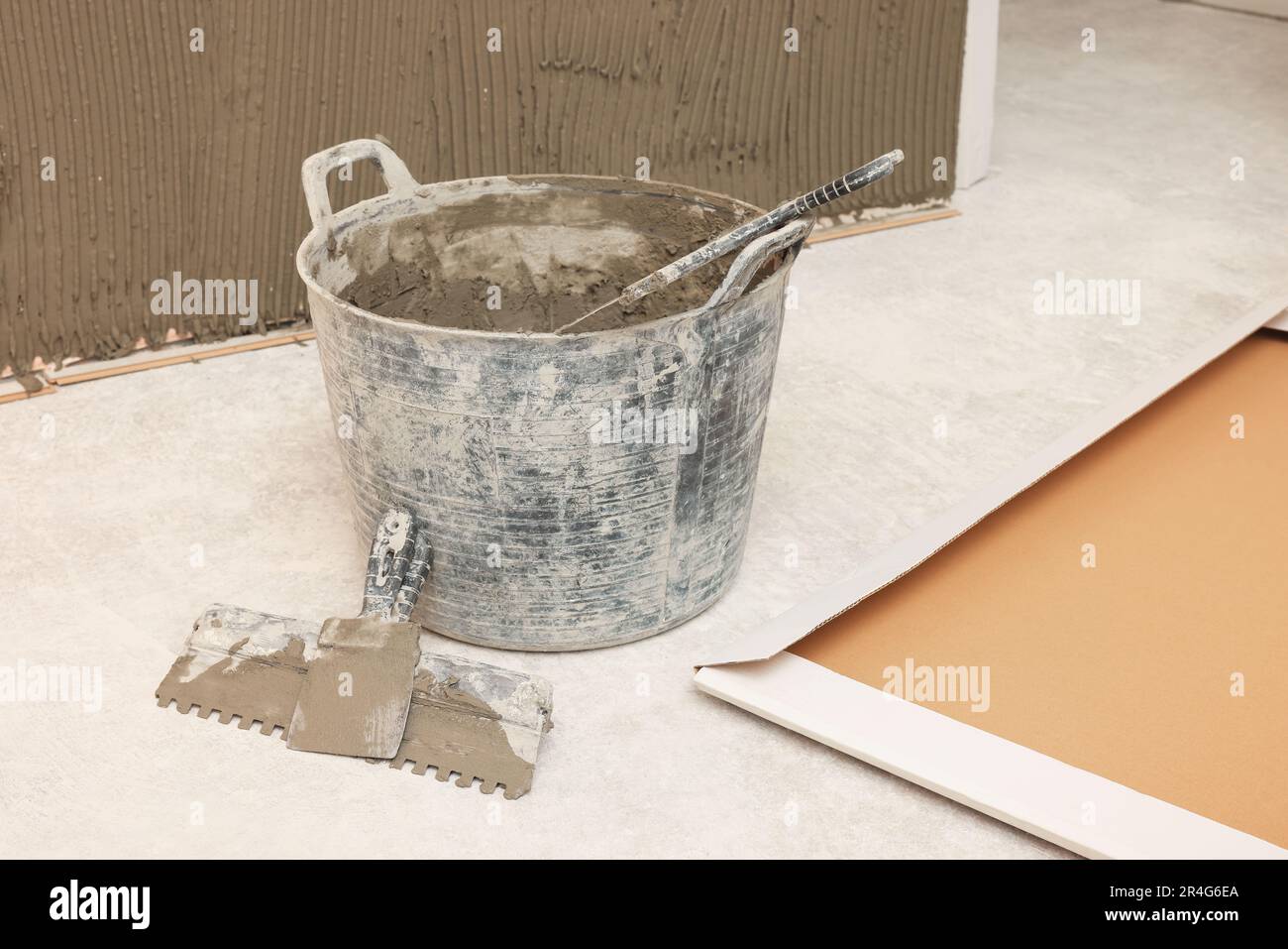Bucket of adhesive mix and spatula on floor indoors Tiles installation ...