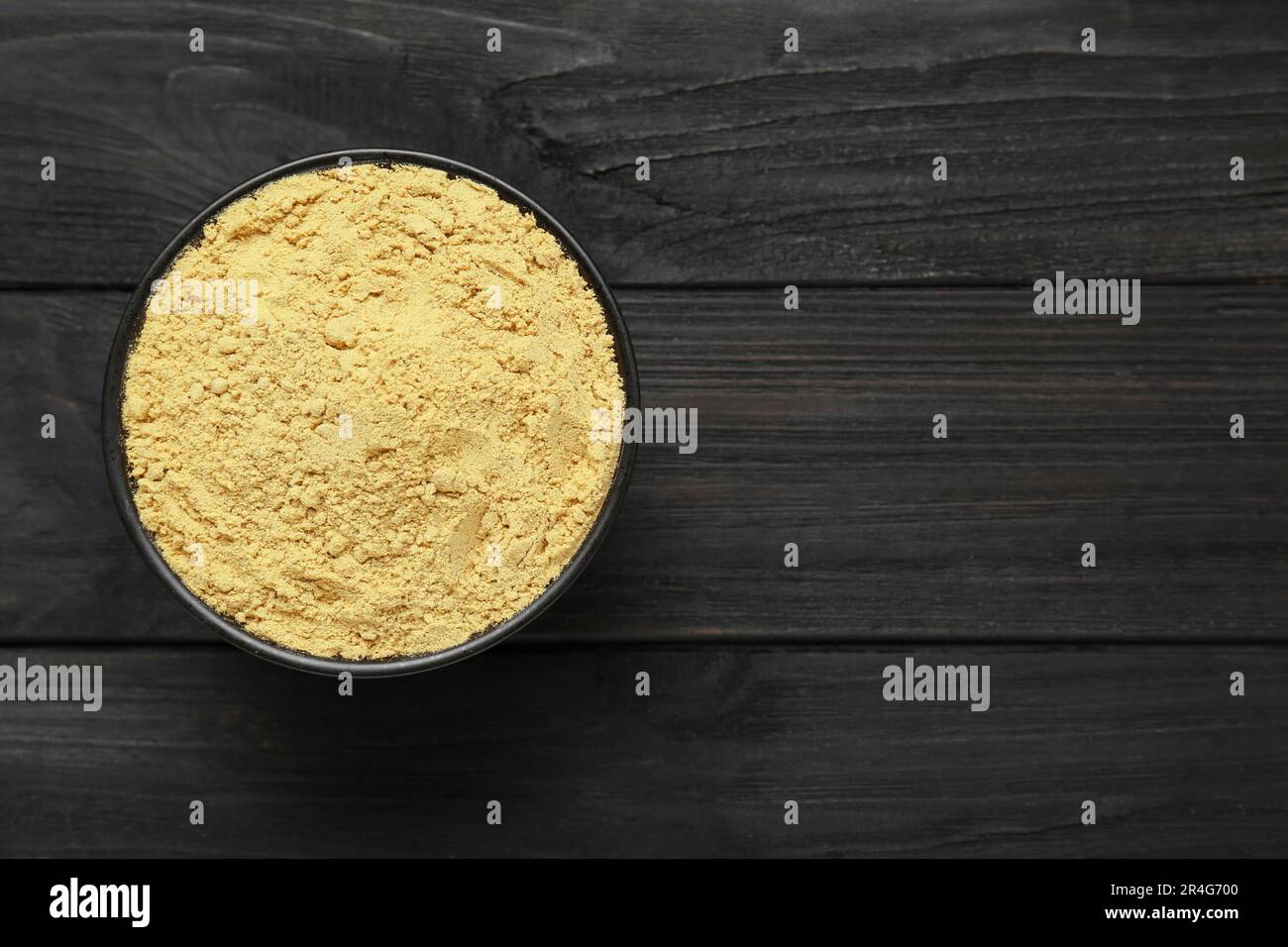 Bowl of aromatic mustard powder on black wooden table, top view. Space ...