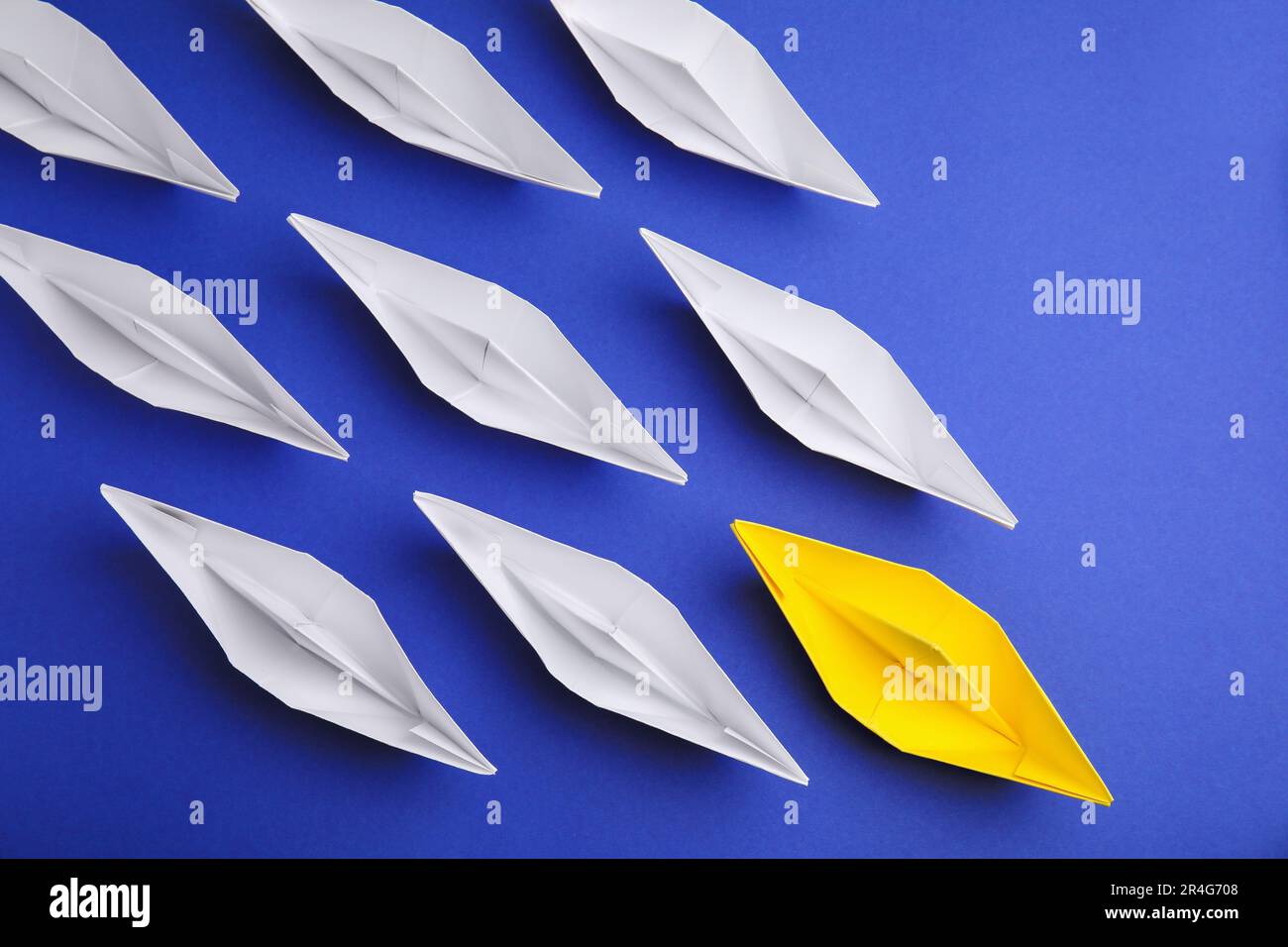 Yellow paper boat leading others on blue background, flat lay ...