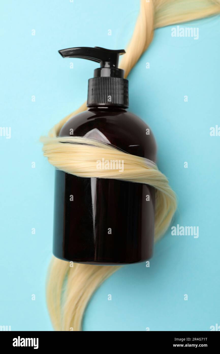 Shampoo bottle wrapped in lock of hair on light blue background, top ...