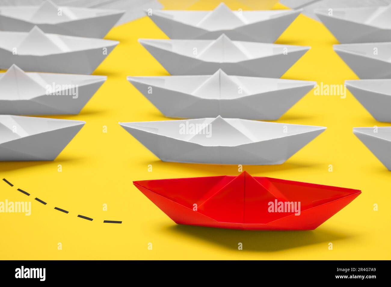 Red paper boat floating away from others on yellow background, closeup ...
