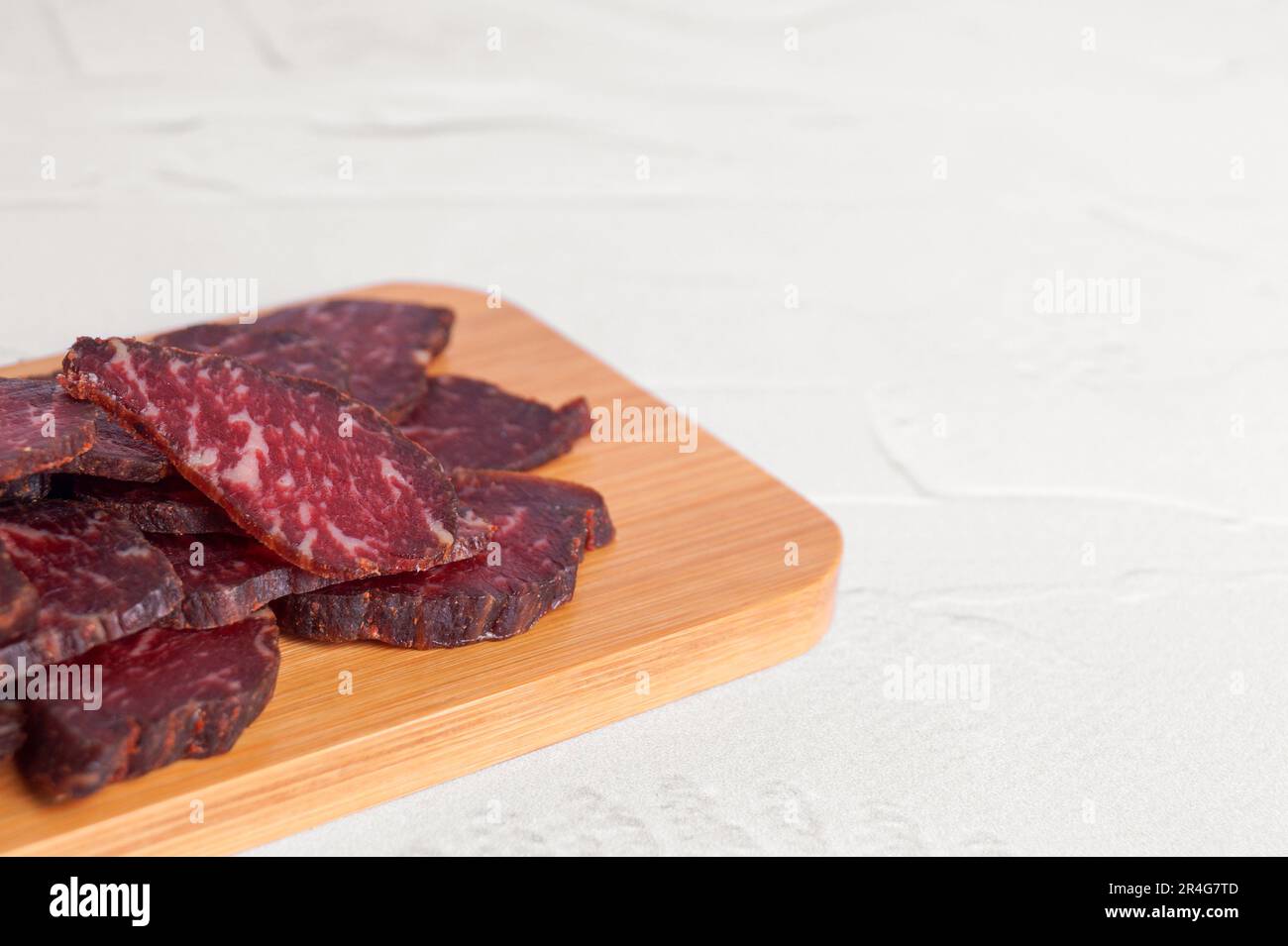 Pieces of delicious beef jerky on white textured table, closeup. Space ...