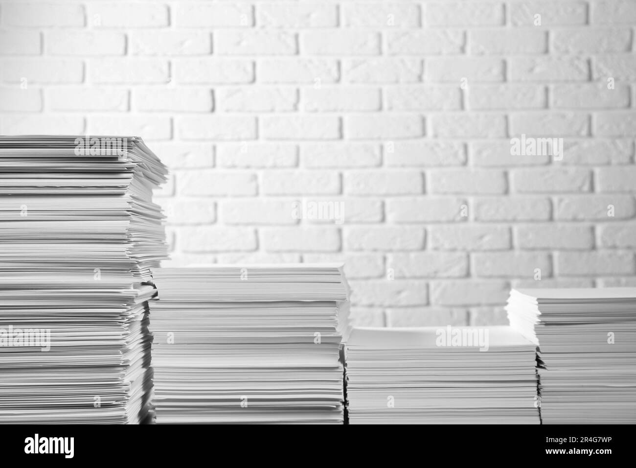 Stacks of paper sheets near white brick wall, space for text Stock ...