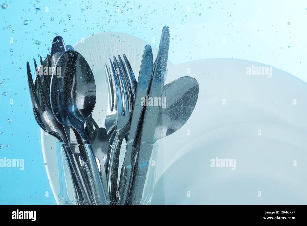 Washing silver cutlery and plates in water on light blue background ...