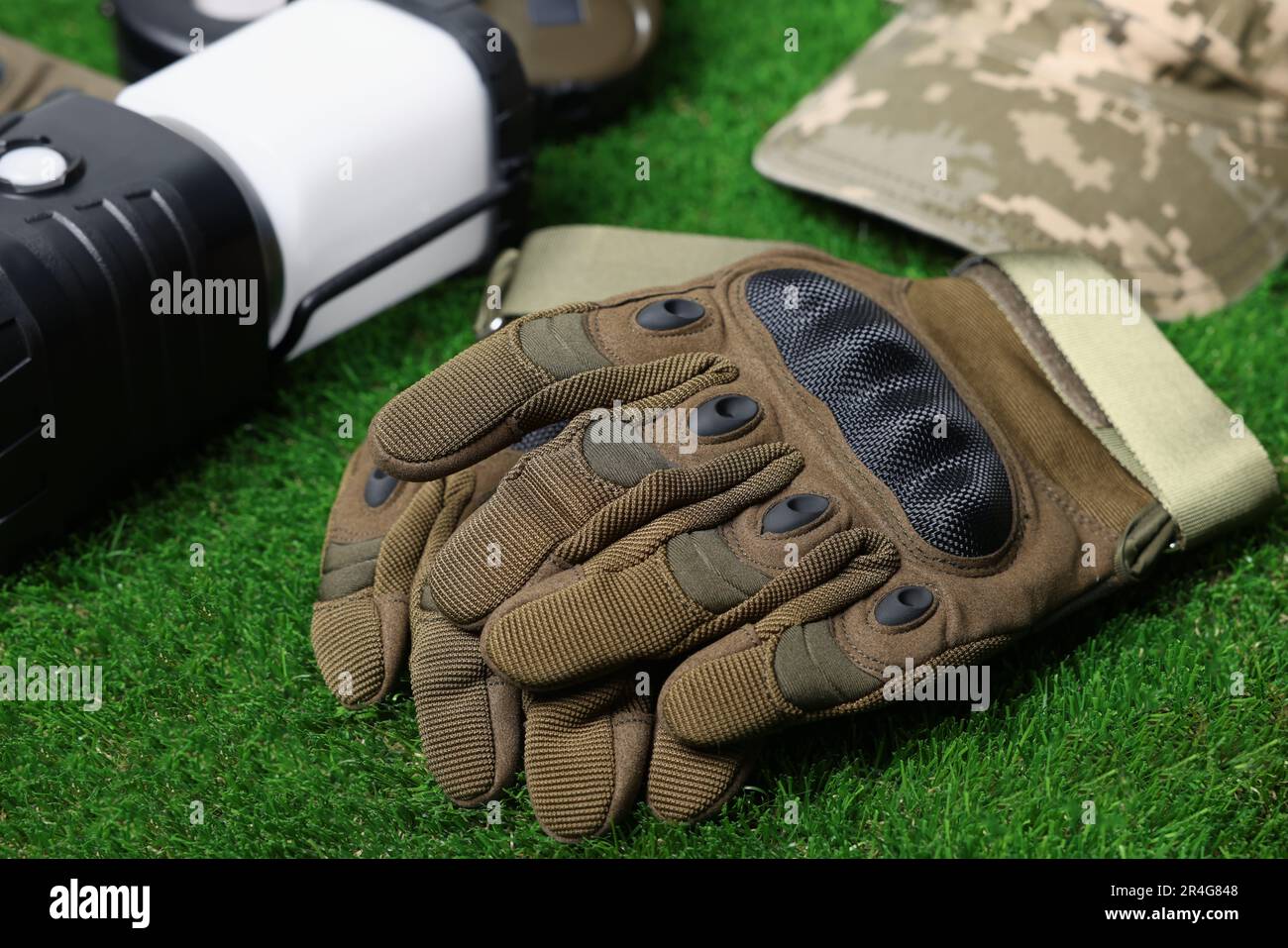 Tactical gloves, camouflage cap and camping lantern on green grass ...