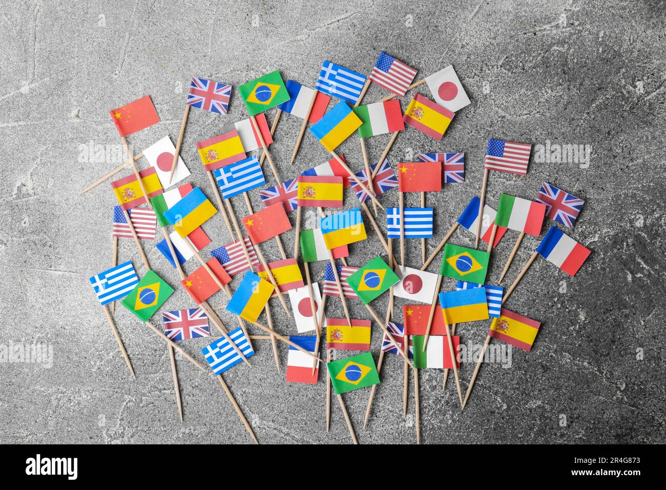 Many small paper flags of different countries on grey table, flat lay ...