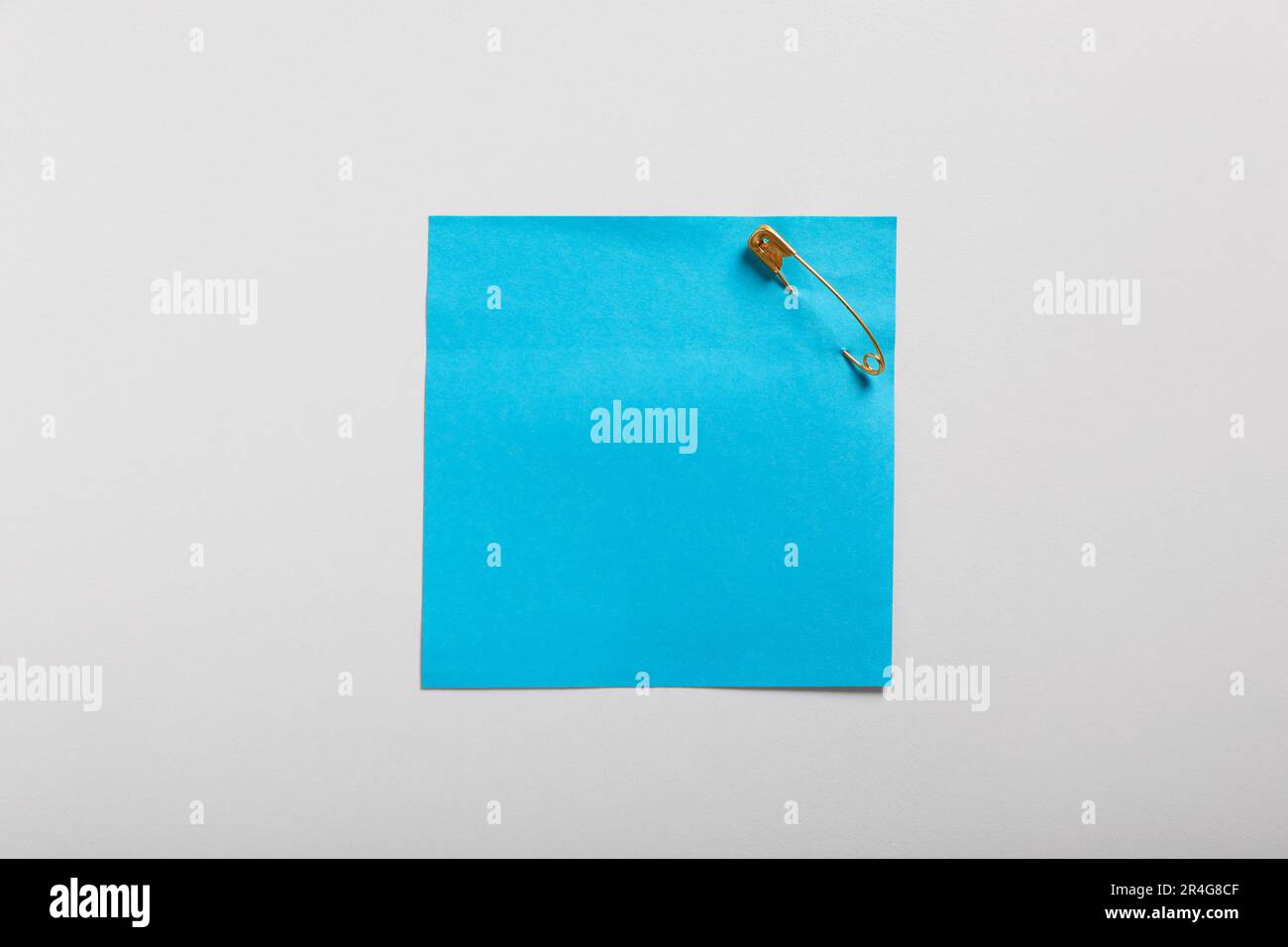 Blue paper note attached with safety pin on white background, top view ...