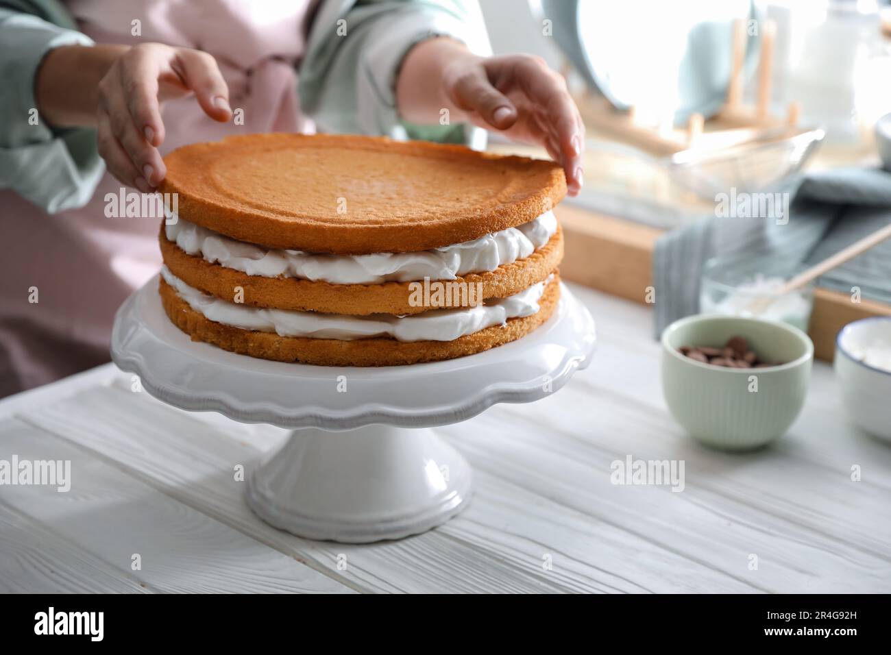 Woman stacking homemade sponge cakes at white wooden table, closeup ...