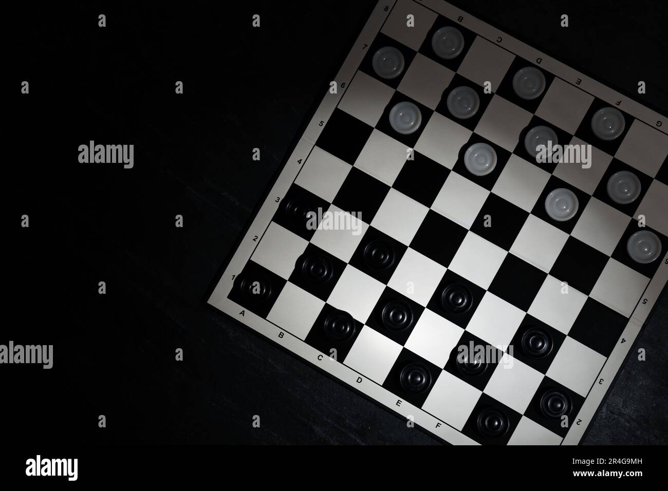Checkerboard with game pieces on black table, top view. Space for text ...
