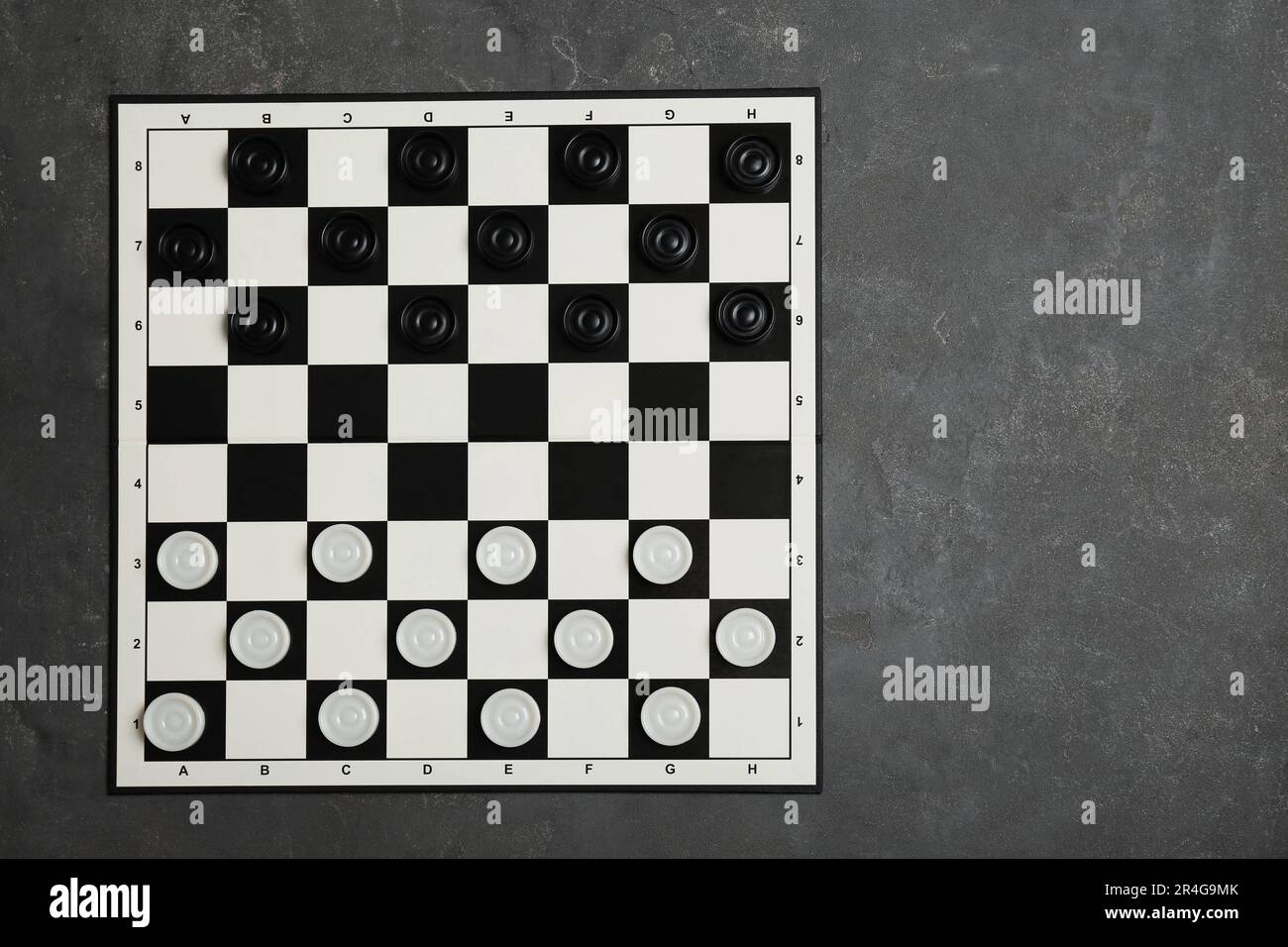 Checkerboard with game pieces on grey table, top view. Space for text ...