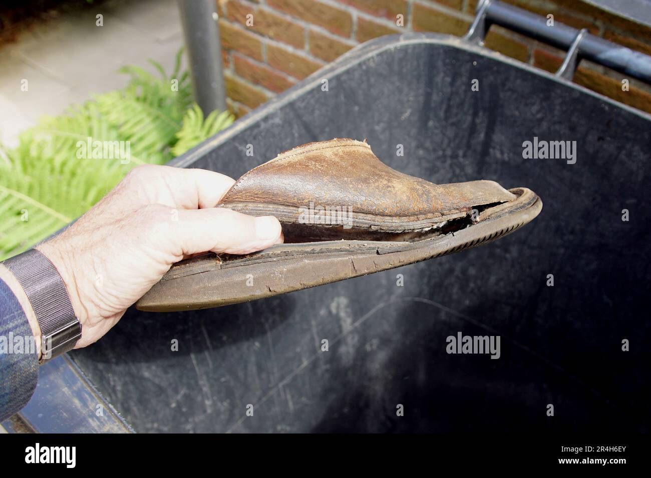 Close up old, broken, brown, worn slipper, shoe. In a garbage container ...