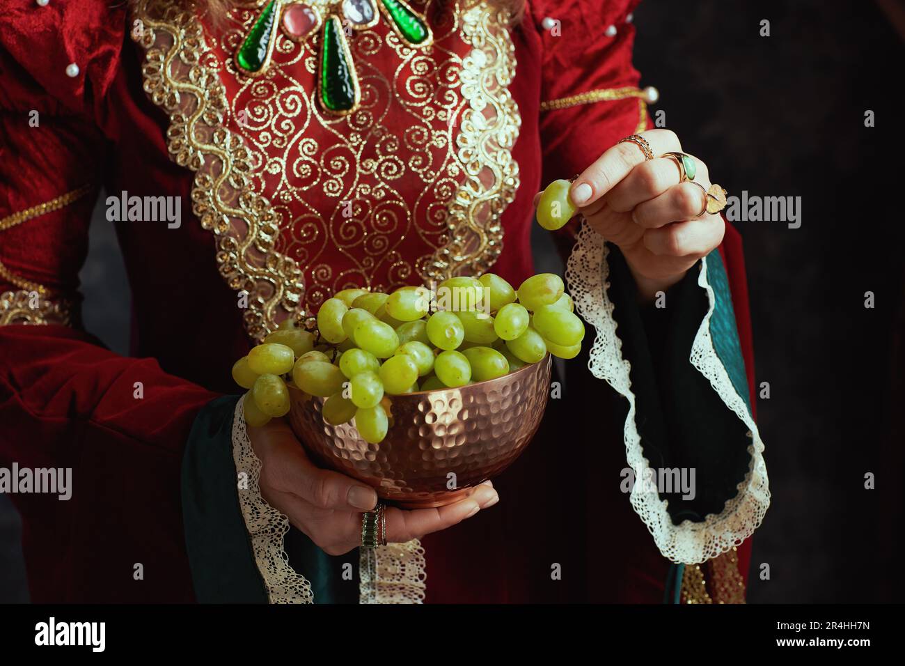 Closeup on medieval queen in red dress with plate of grapes on dark ...