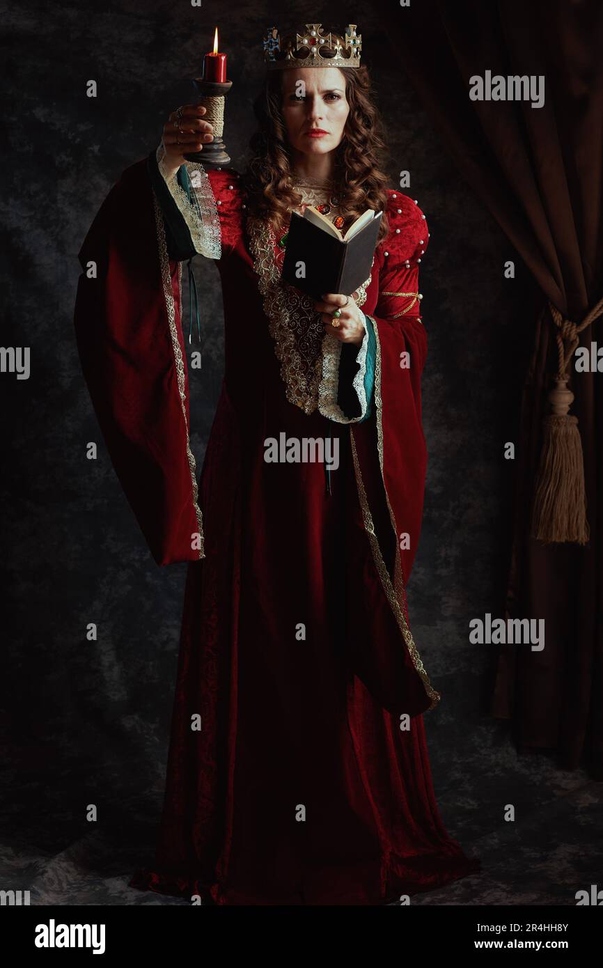 Full length portrait of medieval queen in red dress with book, candle ...