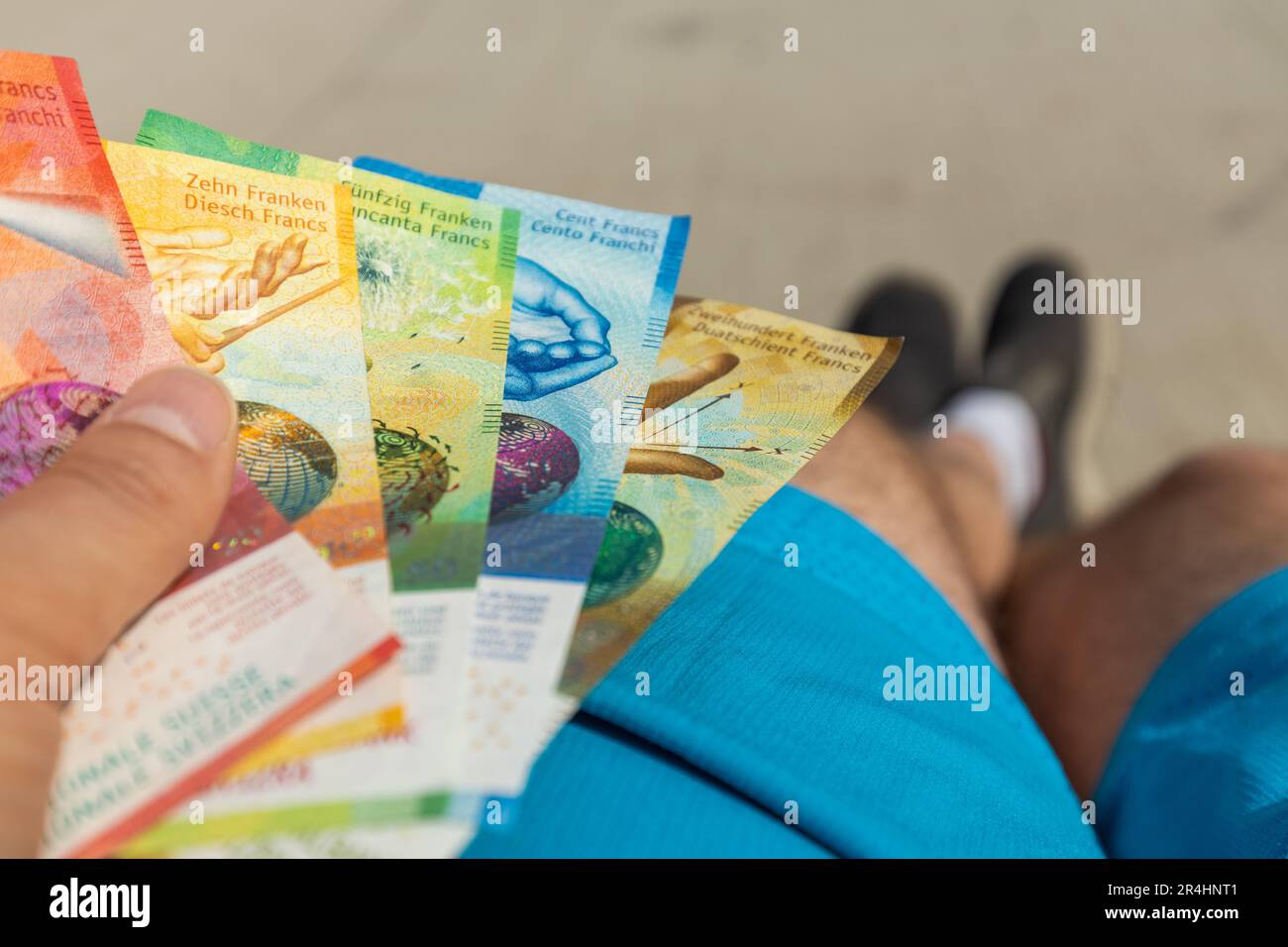 A young man sitting on a bench holds a wad of swiss money in his hand ...