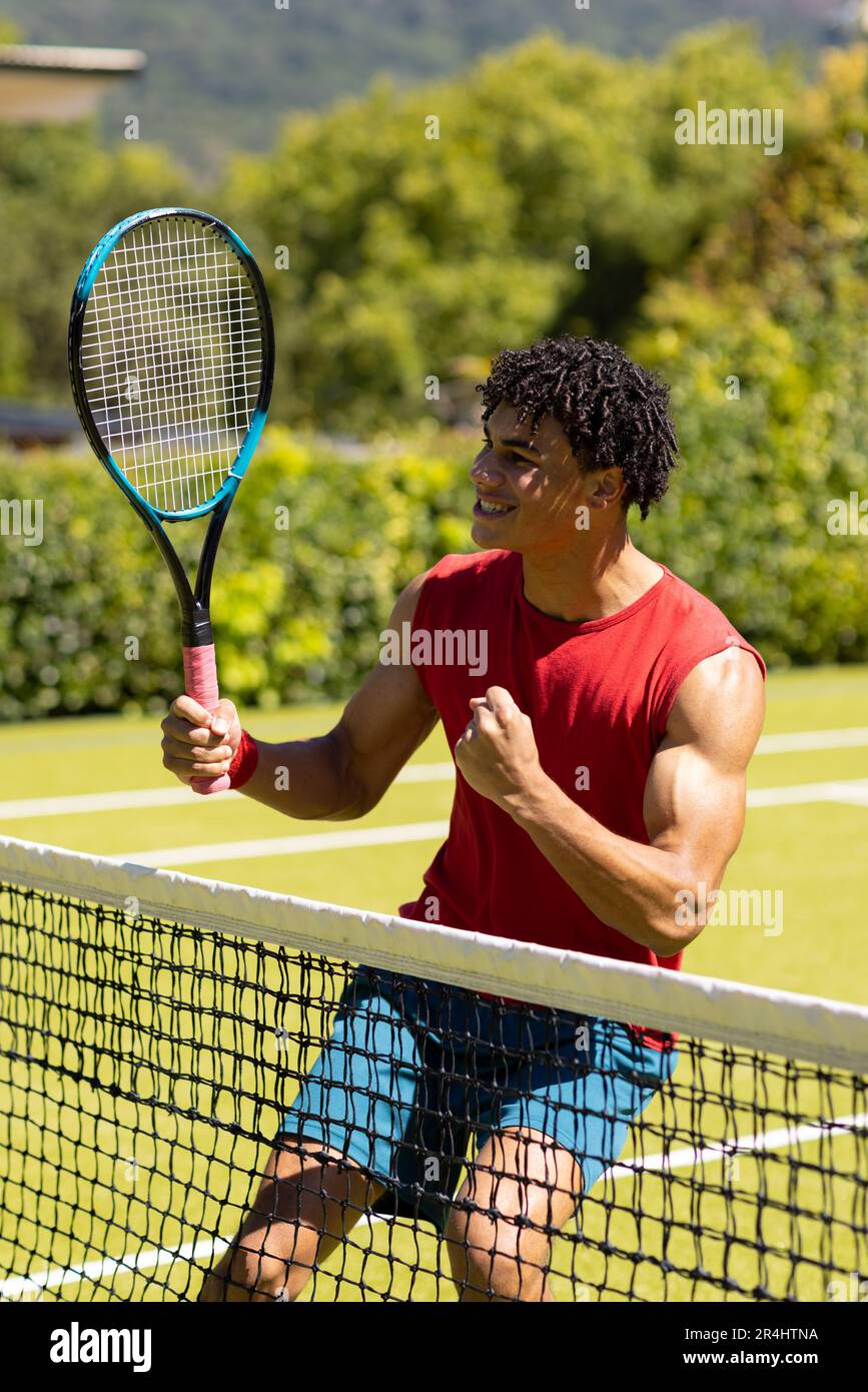 Cheerful biracial young man holding tennis racket pumping fist after ...