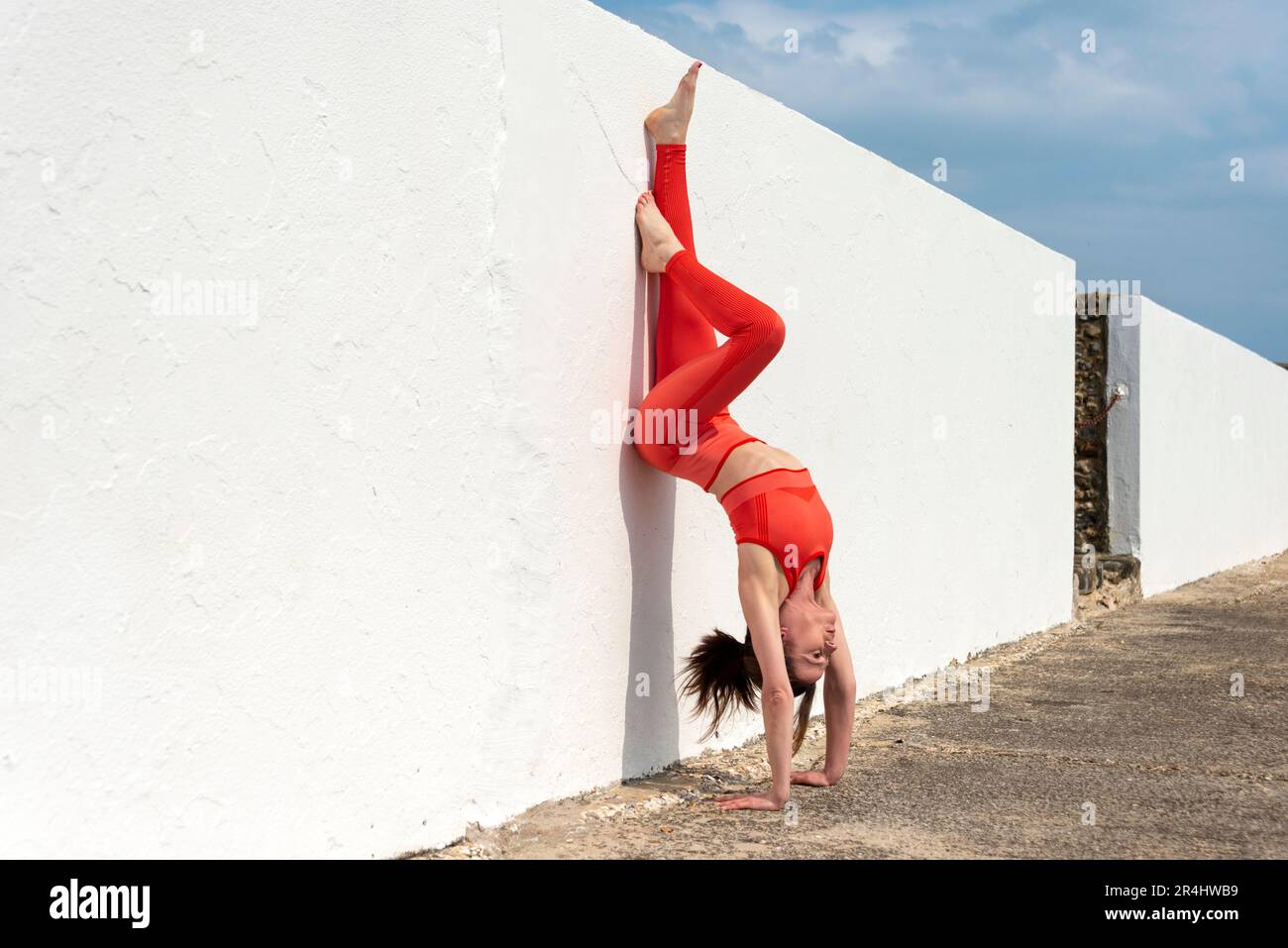 woman doing a handstand against a white wall with blue sky background ...