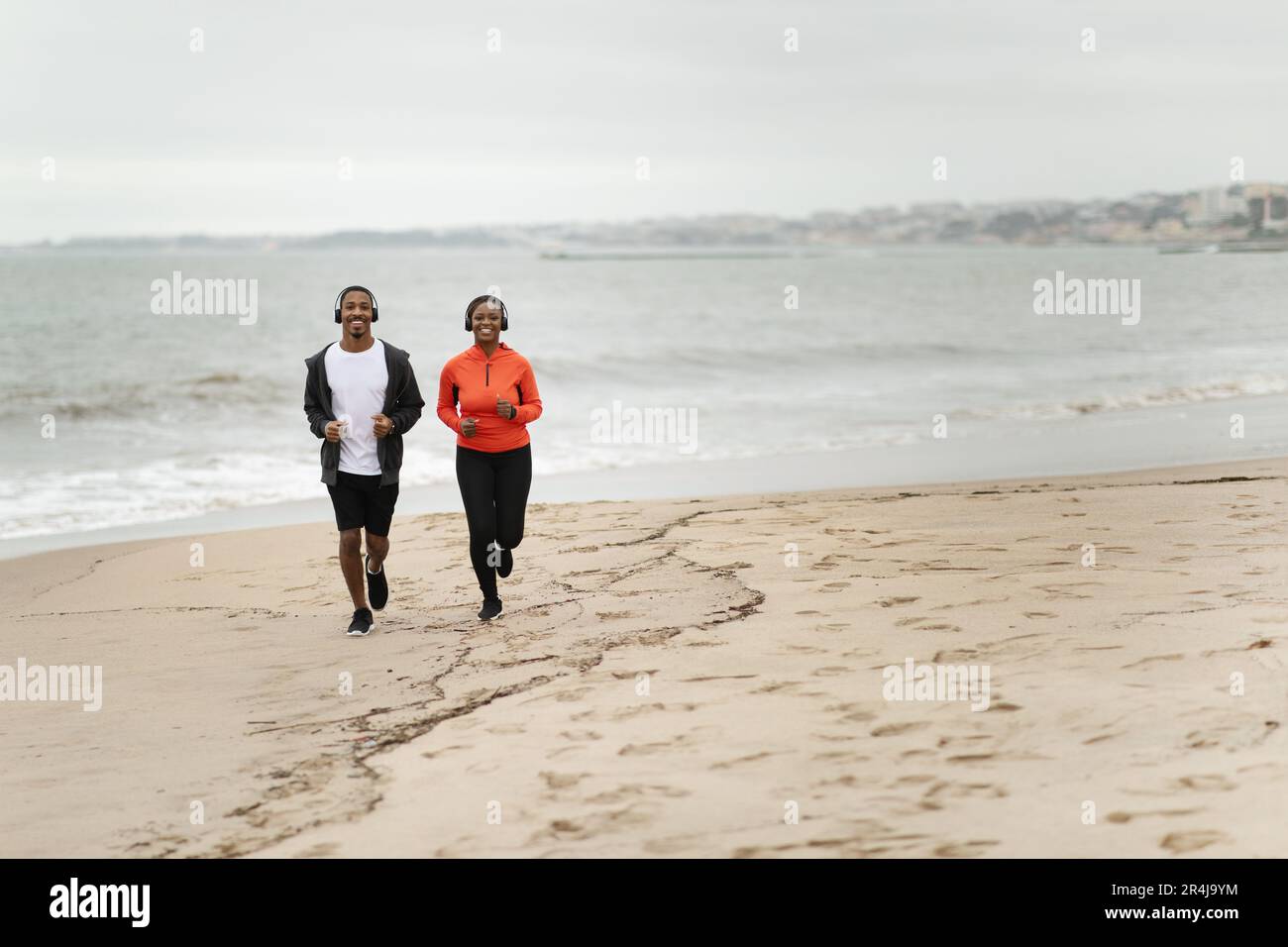 Smiling young black boyfriend and girlfriend in sportswear and wireless ...