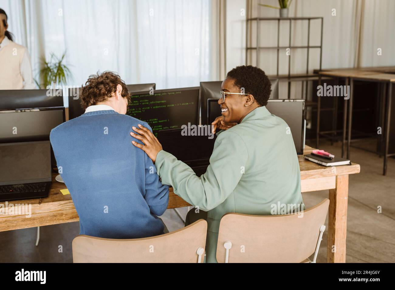 Rear view of smiling female programmer sitting with male colleague at ...