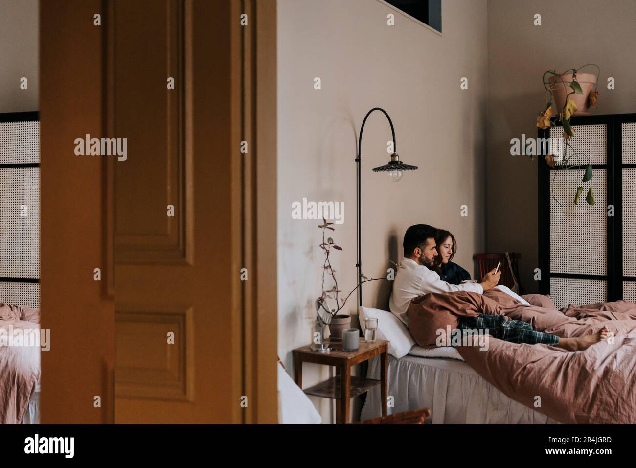 Boyfriend sharing smart phone with non-binary person sitting in bedroom ...