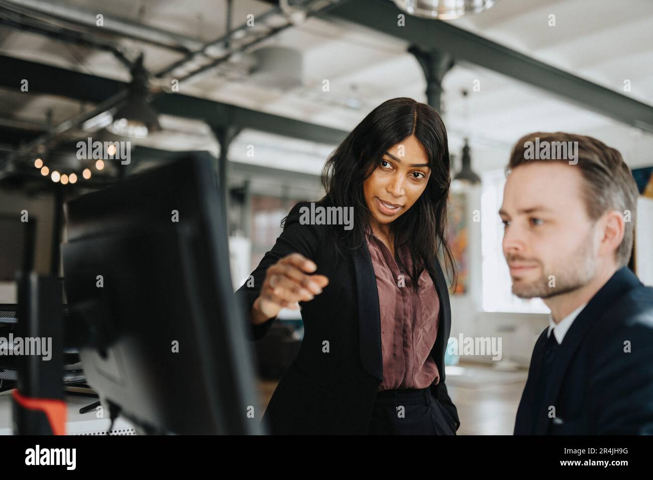 Female entrepreneur explaining male coworker over desktop PC at office ...