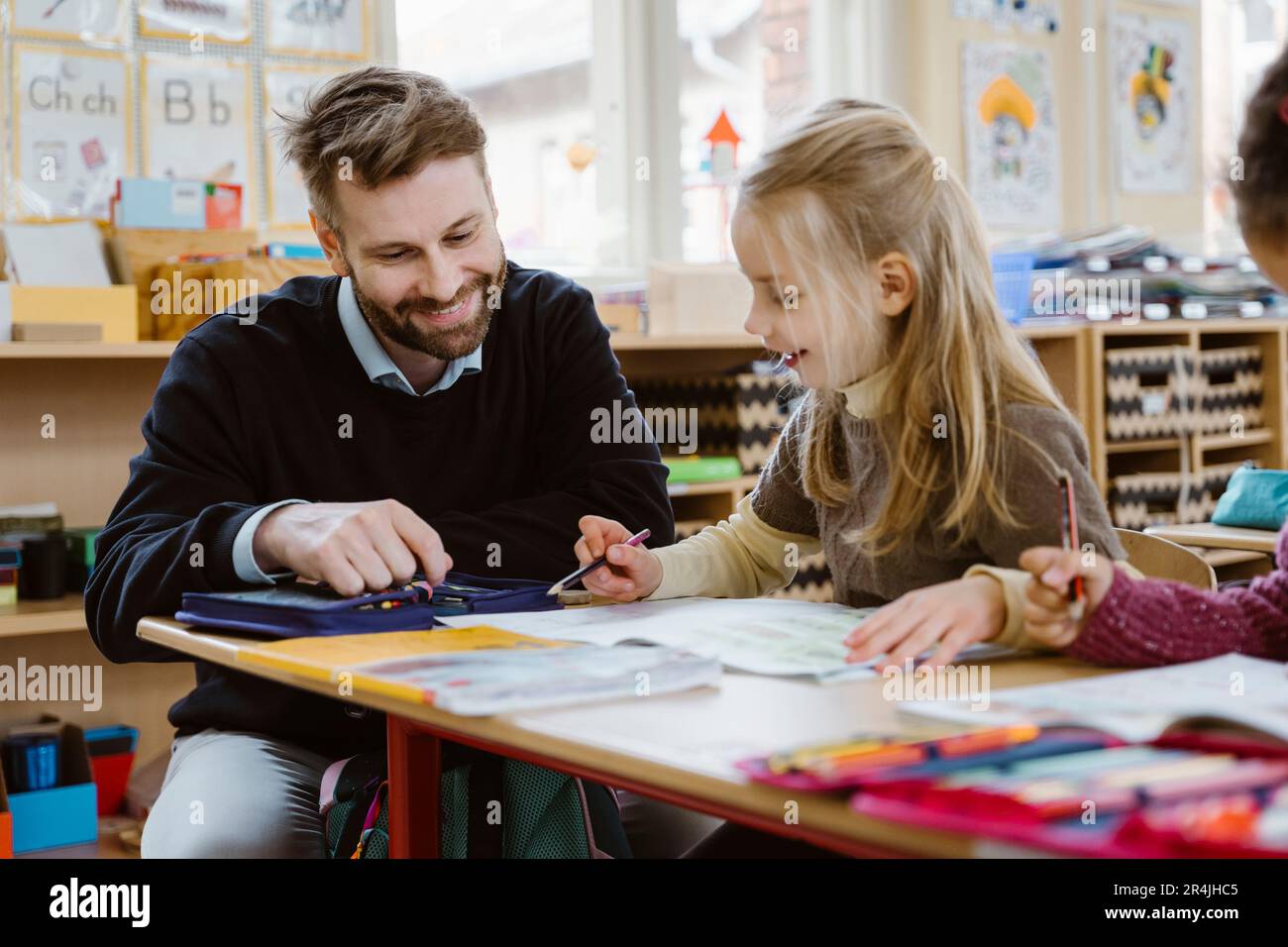 Smiling male teacher assisting female student while studying in ...