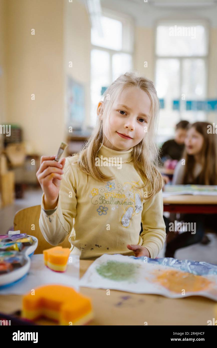 Portrait of female blond student holding paintbrush in classroom Stock ...