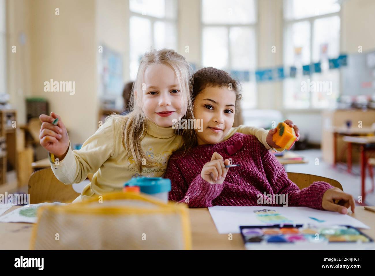 Portrait of schoolgirl with arm around female friend in classroom Stock ...
