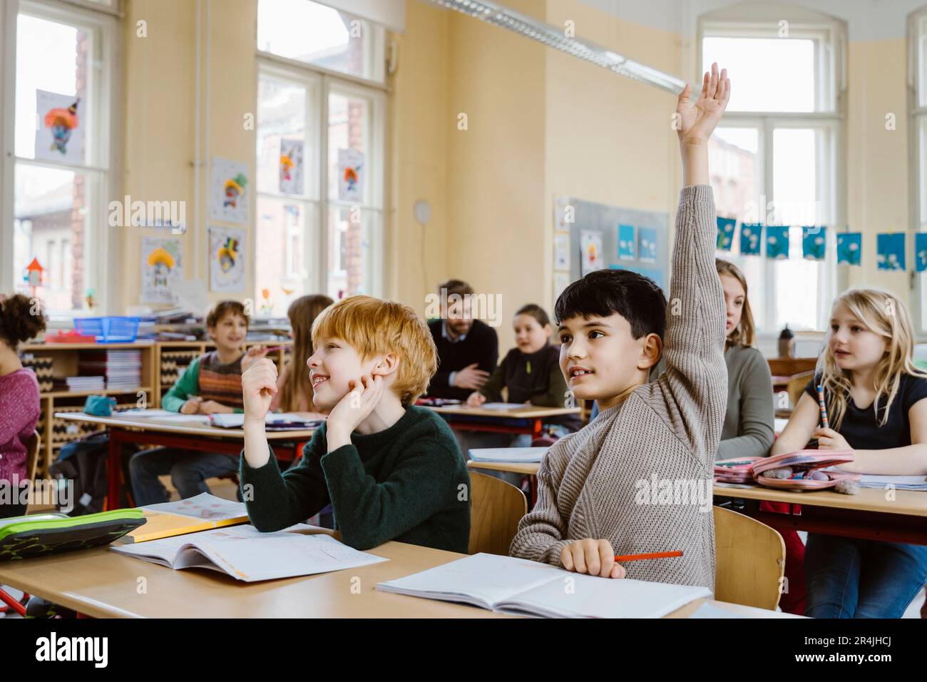 Boy with hand raised answering during lecture while sitting by male ...