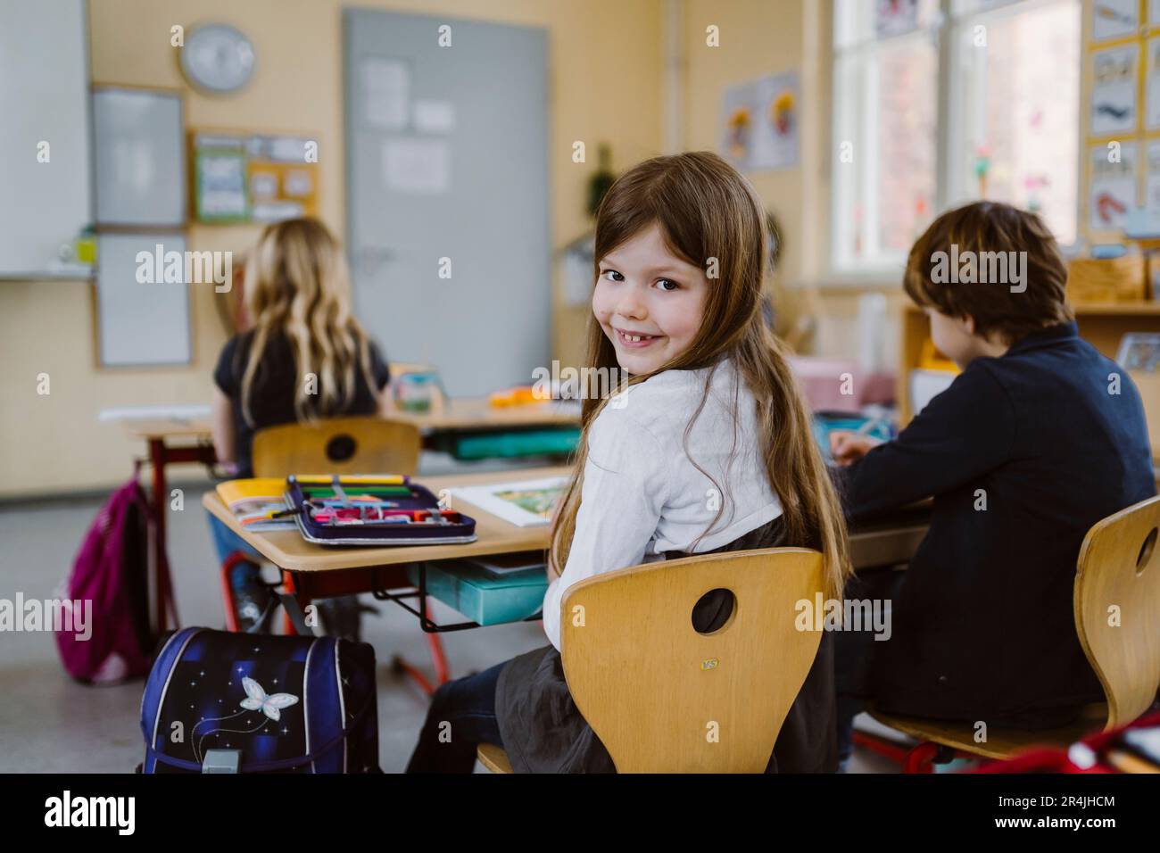 Portrait of smiling girl looking over shoulder sitting on chair by ...