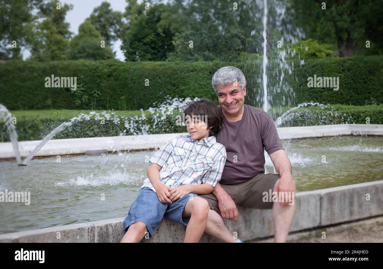 Dad and son are relaxing in the city park near fountains. Family have ...