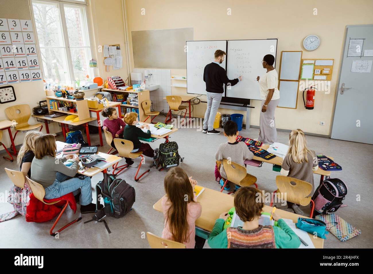 Male and female teachers solving maths problem in front of students in ...