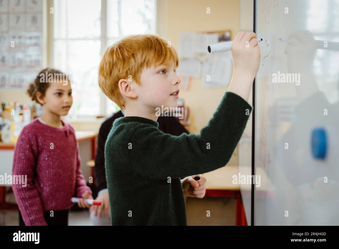 Side view of blond boy writing on whiteboard while solving mathematics ...