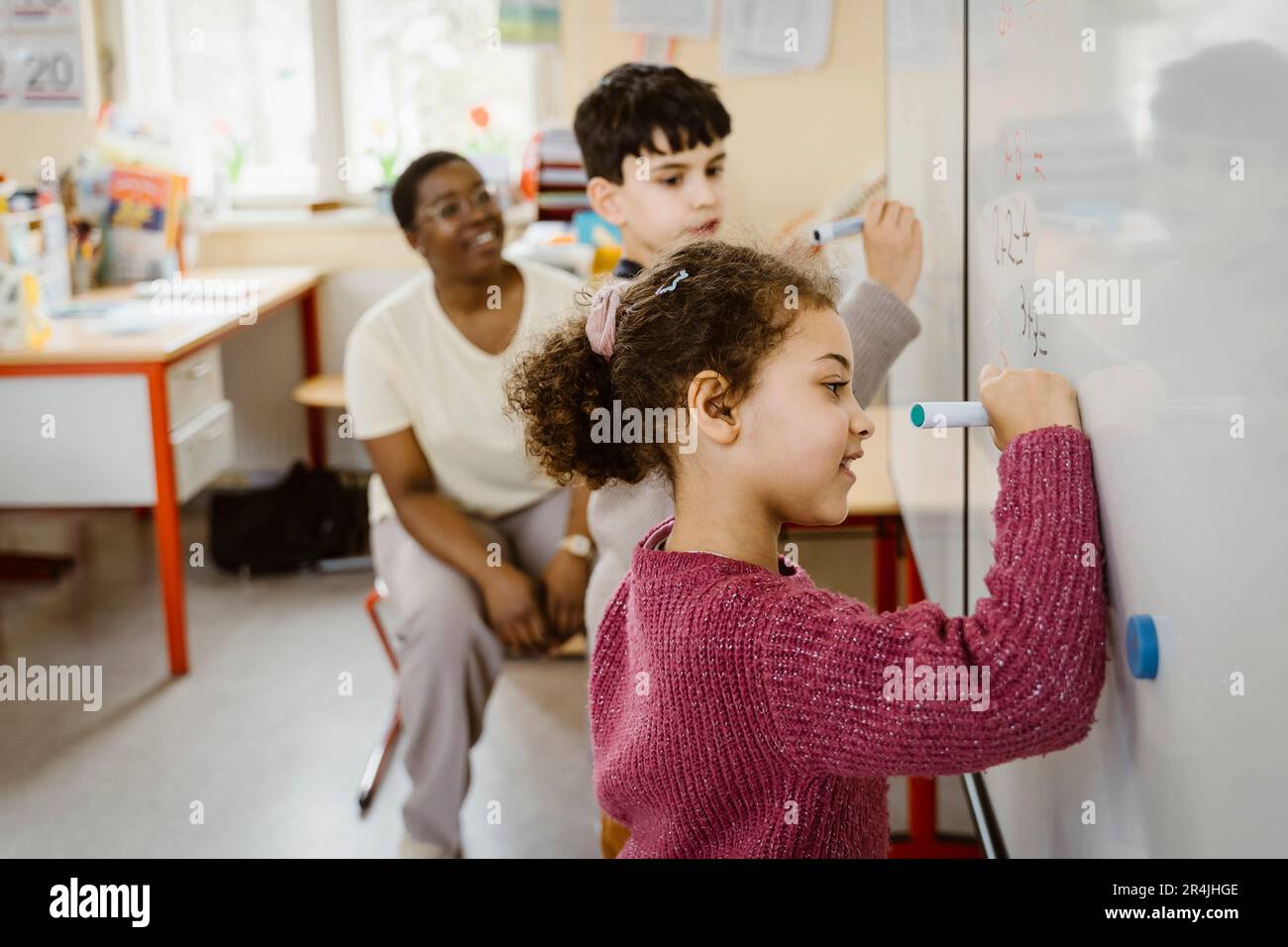 Girl and boy writing on whiteboard while solving mathematics in ...