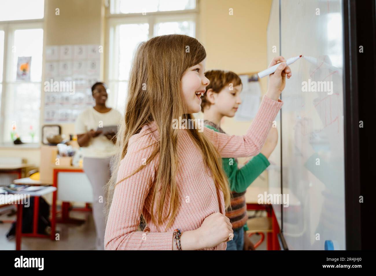 Happy girl writing on whiteboard while solving maths problem in ... Happy girl writing on whiteboard while solving maths problem in ...